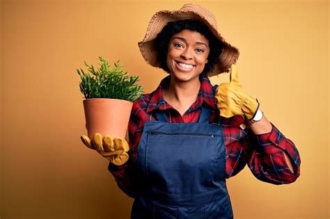 젊은 아프리카계 미국인 농부 여자 곱슬 머리를 입고 앞치마 를 들고 냄비와 식물 행복 한 큰 미소 하 고 확인 기호 손가락으로 엄지 손가락 우수한 기호 명랑한에 대한 스톡