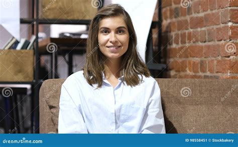 Smiling Young Lovely Girl Sitting On Sofa In Loft Office Stock Image