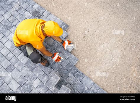 A Construction Worker Is Carefully Placing Gray Paving Stones Onto A Prepared Surface Ensuring