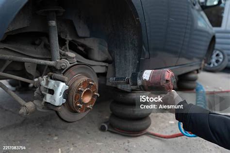 정비사는 임팩트 렌치를 사용하여 들어 올린 차량을 수리하고 노출된 브레이크 구성 요소와 공압 에어 잭 시스템을 보여줍니다 공기 압축기에 대한 스톡 사진 및 기타 이미지