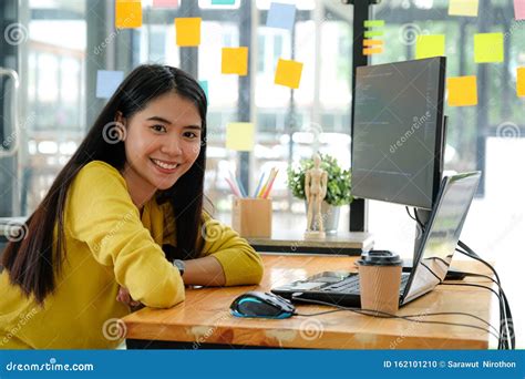 Asian Female Programmer Wearing A Yellow Shirt Sat At Her Desk At The Office She Looked And