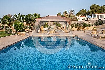 Reflective Blue Pool With A Wooden Pergola And Lounging Chairs In The