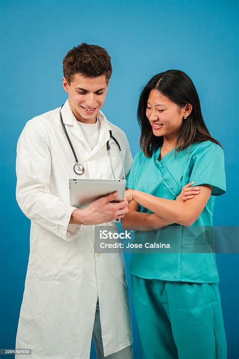 세로 젊은 성인 의사는 파란색 배경 벽에서 진단을 보기 위해 디지털 태블릿을 사용합니다 터치패드를 사용하는 외과 의사 및 심장 전문의 전문가 팀 간호사 및 보조 의사
