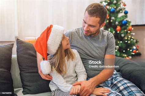 작은 가족 함께 시간을 보내고 그들은 소파에 앉아서 서로 봐 소녀는 크리스마스 모자를 착용 젊은 남자 잠 옷에서입니다 그는 그녀를 포용 그들은 행복 하 게 보세요 12월에