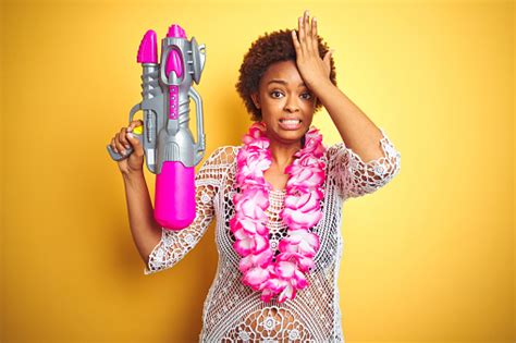 꽃 하와이 레이와 물 총을 입고 아프리카 계 미국인 젊은 여성은 부끄러움과 깜짝 얼굴 분노와 좌절에 충격 머리에 손으로 스트레스 실수에 대한 두려움과 화가 실망에 대한 스톡