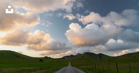 낮에는 흰 구름 아래 푸른 잔디밭과 푸른 하늘 사이의 회색 아스팔트 도로 사진 Unsplash의 무료 길 이미지