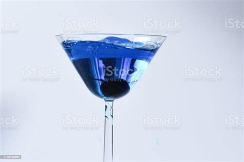 유리에 푸른 액체와 칵테일 물튀김과 방울로 액체를 붓는 푸른 물이있는 유리 흰색 배경에 스플래시와 알코올로 채우는 마티니 유리