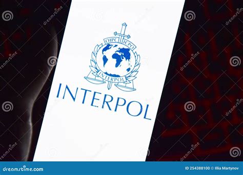 A Smartphone With The Interpol Logo Displayed On The Screen Lies On The