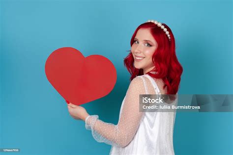 클로즈업 행복한 웃음 여자는 흰색 드레스와 파란색 배경에 고립 된 큰 빨간 종이 심장을 들고 빨간색 머리를 입고 프로필에 서 20 24세에 대한 스톡 사진 및 기타 이미지