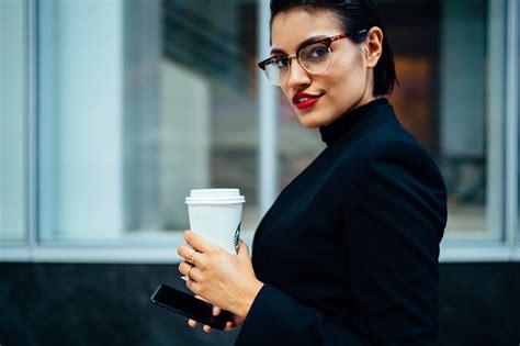 도심에서 커피 휴식 중 카메라를 보고 성공적인 여성 전문가의 절반 길이 초상화 도시 설정에 서 손에 새로운 휴대 전화와 긍정적