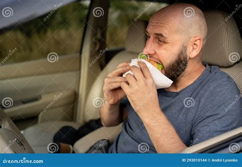 Happy Man Driver Eating A Fresh Burger While Driving A Car The Concept Of Ordering Fast Food