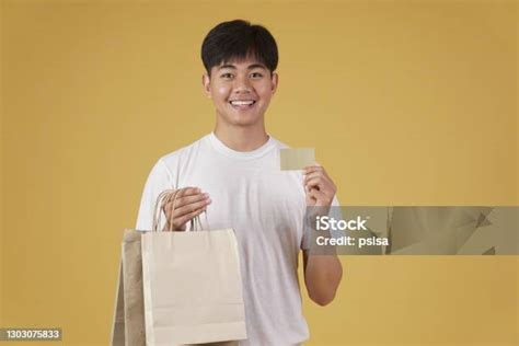 노란 배경에 고립 된 쇼핑 백과 신용 카드를 들고 캐주얼 옷을 입은 행복한 젊은 아시아 남자의 초상화 20 24세에 대한 스톡
