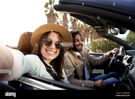 Caucasian Young Couple Driving A Cabrio Car Woman Takes Selfie With
