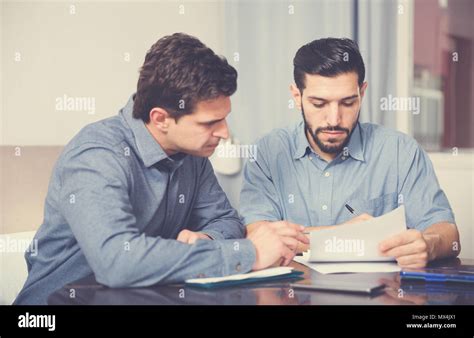 Two Young Men In Serious Discussion At Home Table While Analysing