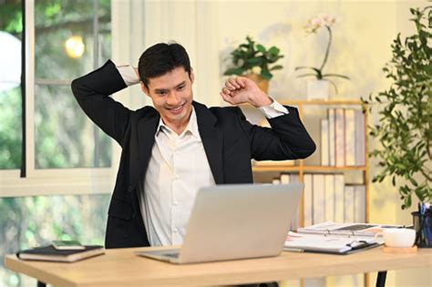 바쁜 근무일 동안 책상에 앉아 휴식을 취하면서 팔을 뻗고 있는 웃는 성인 사업가 30 34세에 대한 스톡 사진 및 기타 이미지