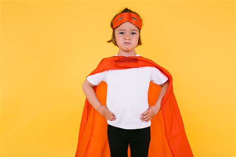 작은 금발 소녀 케이프와 빨간 마스크와 슈퍼 히어로로 옷을 입고 화가 그녀의 팔 Akimbo 심각한 노란색 배경에 4 5세에