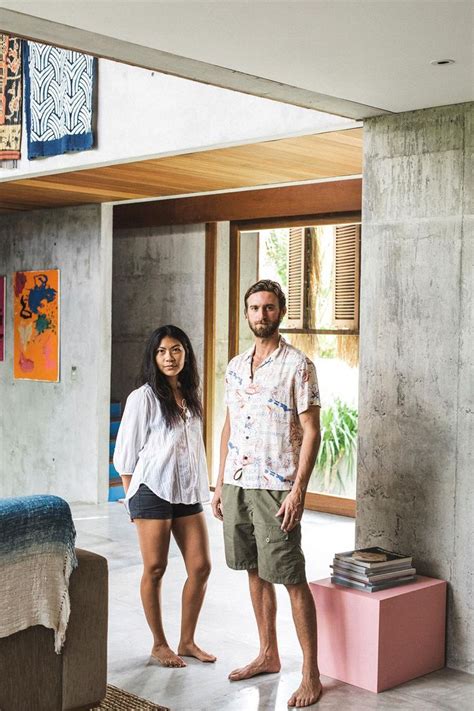 A Man And Woman Standing Next To Each Other In A Living Room With Concrete Walls
