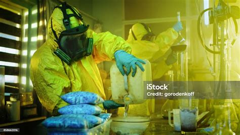 지 하 약 실험실 보호 마스크와 작업복을 입고 은밀한 화학자 화학 혼합 하나는 그릇 제품 일관성에 대 한 두 번째 검사 비 커에 용기에서 액체를 부 어 넣는다 그들은