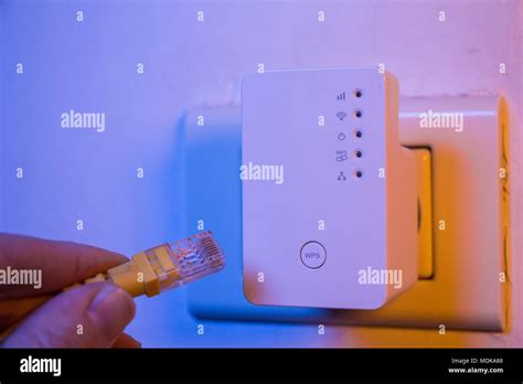 Man Insert Ethernet Cable Into WiFi Extender Device Which Is In Electrical Socket On The Wall