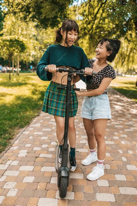 Premium Photo Cute Slim Young Girls Riding A Scooter In The Park