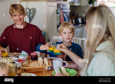 Family eating breakfast together in home kitchen, toasting with juice. Healthy breakfast or ...