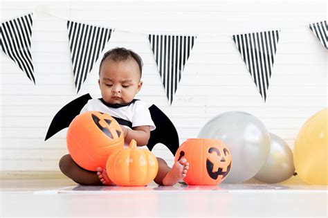 검은 박쥐 날개가있는 뱀파이어 멋진 할로윈 의상을 입은 사랑스러운 아프리카 아기 아이 쾌활한 작은 귀여운 아이는 오랑 호박