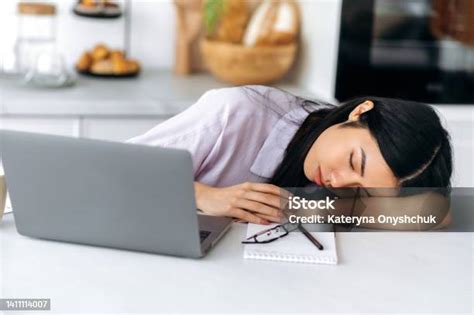 졸린 중국 민족 젊은 여성 부엌에서 집에서 노트북 근처 직장에 앉아있는 동안 잠들고 지루한 직업에 지치고 과로하고 만성 수면 부족을 경험하고 휴식이 필요합니다 잠자기에 대한
