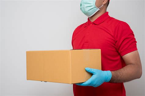 마스크와 고무 장갑을 착용한 빨간 배달 남자를 닫고 고객에게 보내는 소포 상자 골판지를 보관하는 것은 주의와 안전 전달
