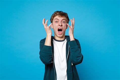 짜증나는 화가 충격 젊은 남자의 초상화 상승 비명 스튜디오에서 파란색 배경에 고립 된 손을 확산 사람들은 진심으로 감정 라이프 스타일 개념입니다 복사 공간을 모의 합니다 T