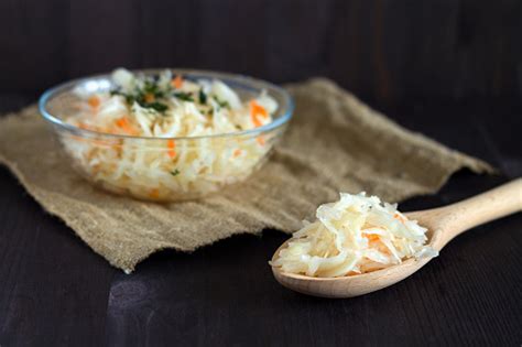 검은 색 배경에 유리 접시에 허브와 당근과 수제 소금에 절인 양배추 나무 테이블에 자루천이 있는 숟가락에 양배추를 절인 양배추 통조림 식품의 개념 복사 공간을 복사합니다