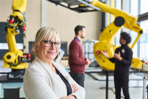Confident Woman In Robotics Laboratory With Colleagues Discussing Automation Processes Stock