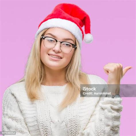 젊은 백인 여자 생기고 엄지 측면 가리키는 행복 한 얼굴로 웃 고 고립 된 배경 위에 크리스마스 모자를 쓰고 가리키기에 대한 스톡 사진 및 기타 이미지 Istock