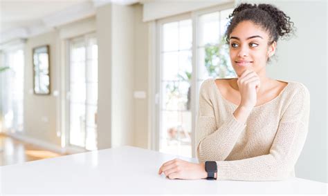 집에서 테이블에 앉아 아프리카 머리와 아름 다운 젊은 아프리카계 미국인 여자는 교차 팔과 손 턱에 제기와 미소와 함께 카메라에 자신감을 찾고 긍정적 인 생각 가정 생활에