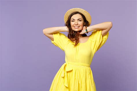 노란색 드레스 여름 모자 카메라를 찾고 웃는 젊은 여자 스튜디오에서 파스텔 바이올렛 벽 배경에 고립 된 목에 손을 넣어 사람들은 진심으로 감정 라이프 스타일 개념입니다 복사