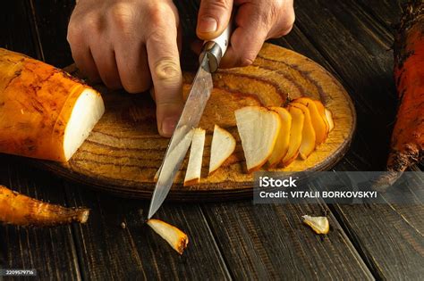 신선한 고구마를 소박한 나무 도마에 솜씨 좋게 얇게 썰어 올려 손이 솜씨 좋게 썰어줍니다 주방 환경은 따뜻하고 매력적으로 식사