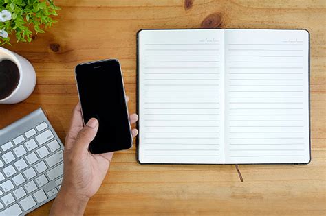 바로 위의 사진 사무실의 책상에서 열린 일기 위에 스마트 폰을 사용하여 자른 손의 샷 Brand Name Smart Phone에 대한 스톡 사진 및 기타 이미지