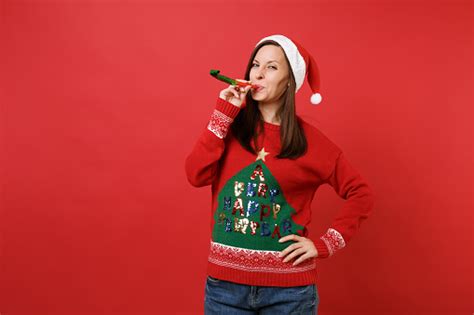 즐거운 산타 소녀 니트 스웨터와 크리스마스 모자 재생 파이프에 불고 밝은 빨간 벽 배경에 고립 행복 한 새 해 2019 축 하 휴일 파티 개념입니다 복사 공간을 비웃는 다