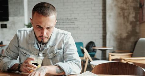 데님 재킷을 입은 젊은 수염 난 남자가 카페에 앉아 차가운 커피를 마시며 지도를 사용하여 방문하기 가장 좋은 장소를 찾고 있다 사진 Unsplash의 앉아 이미지