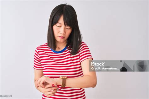 젊은 아름다운 중국 여자 입고 빨간 줄무늬 티셔츠 위에 고립 된 흰색 배경 손목 시계에 시간을 확인 편안하고 자신감 T 셔츠에 대한 스톡 사진 및 기타 이미지 Istock