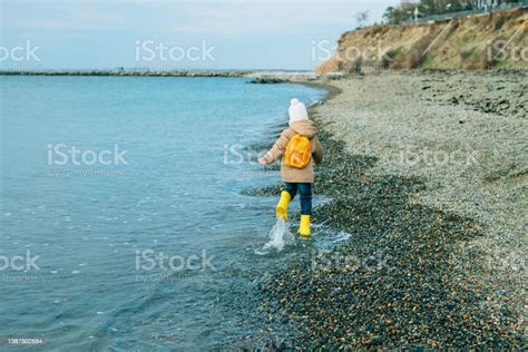 어린 소녀는 바터웨어와 고무 부츠를 입고 가을에 바다의 바위 해안을 따라 달리고 있습니다 한 어린이가 바다 의 해변을 따라 달리고 발로 물을 때리고 물 튀김을 만듭니다 6