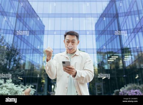 Happy Asian Man Celebrating Victory And Success Holding Phone Smiling