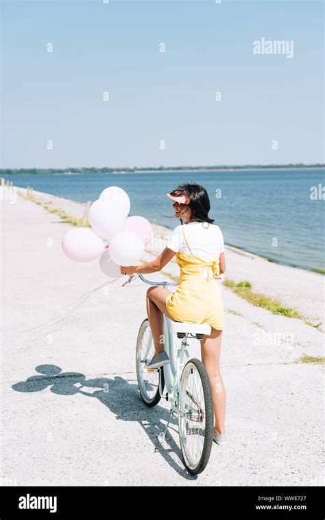 Back View Of Beautiful Brunette Girl Riding Bike With Balloons Near
