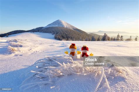 눈 덮인 들판에 빨간 모자와 스카프를 입은 두 명의 작은 눈사람 아름다운 겨울 일몰 배경 높은 산과 풍경 메리 크리스마스와 새해 복 많은 새해 0명에 대한 스톡 사진 및