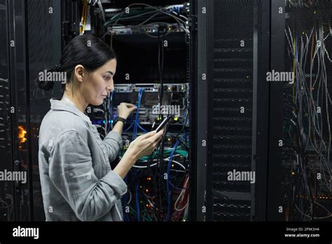 Side View Portrait Of Female Network Technician Connecting Cables In Server Cabinet While