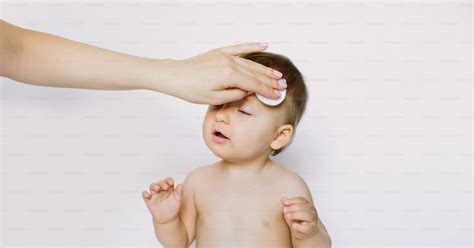 어머니 손은 흰색 배경에 면봉으로 1 년 여자 아기의 얼굴을 청소합니다 아기 위생 관리 건강 관리 의료 개념 사진