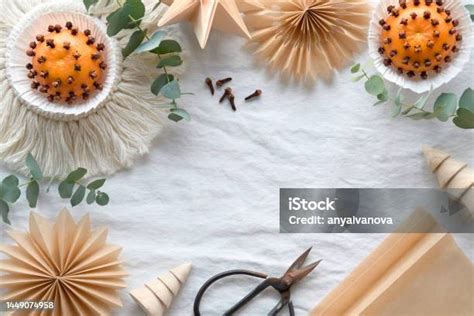 향기로운 포맨더 볼 감귤과 정향으로 손수 만든 갈색 베이킹 페이퍼로 만든 수제 종이 별 향기로운 녹색 유칼립투스 나뭇 가지가있는 흰색 섬유 식탁보에 평평하게 누워 있습니다