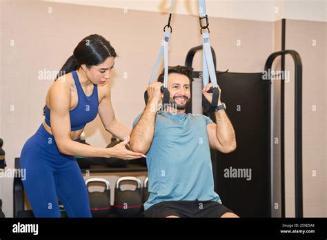 Personal trainer guiding a client through suspension exercises in a gym ...