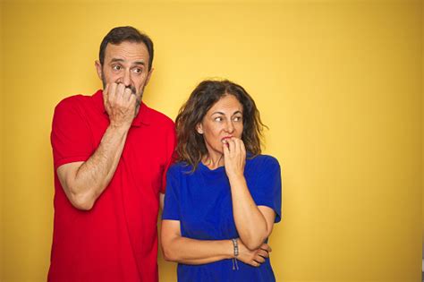 아름다운 중년 부부는 함께 입물고 손톱에 손을 긴장 찾고 고립 된 노란색 배경 위에 서 불안 문제 2명에 대한 스톡 사진 및 기타 이미지 Istock