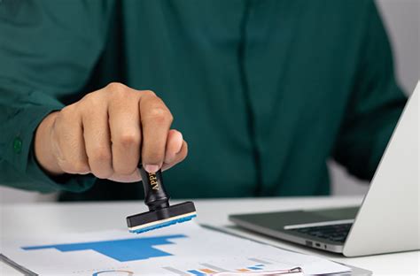 책상에서 승인된 문서에 승인된 스탬프가 찍힌 사업가의 클로즈업 비즈니스 문서 및 계약 계약 양식 용지를 확인 및 관리합니다 승인 스탬프 개념에 대한 스톡 사진 및 기타