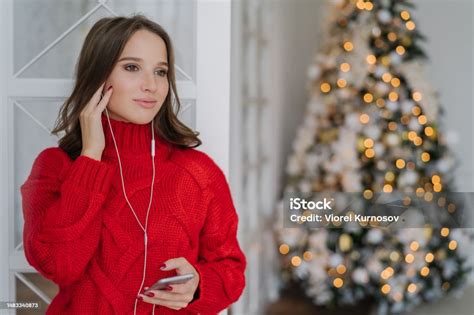 사람 휴일 및 기술 개념 예쁜 여자는 음악을 듣고 휴대 전화와 이어폰을 사용 텍스트에 대한 복사 공간이 크리스마스 트리 조명 배경에 대해 집에서 서 20 24세에 대한 스톡